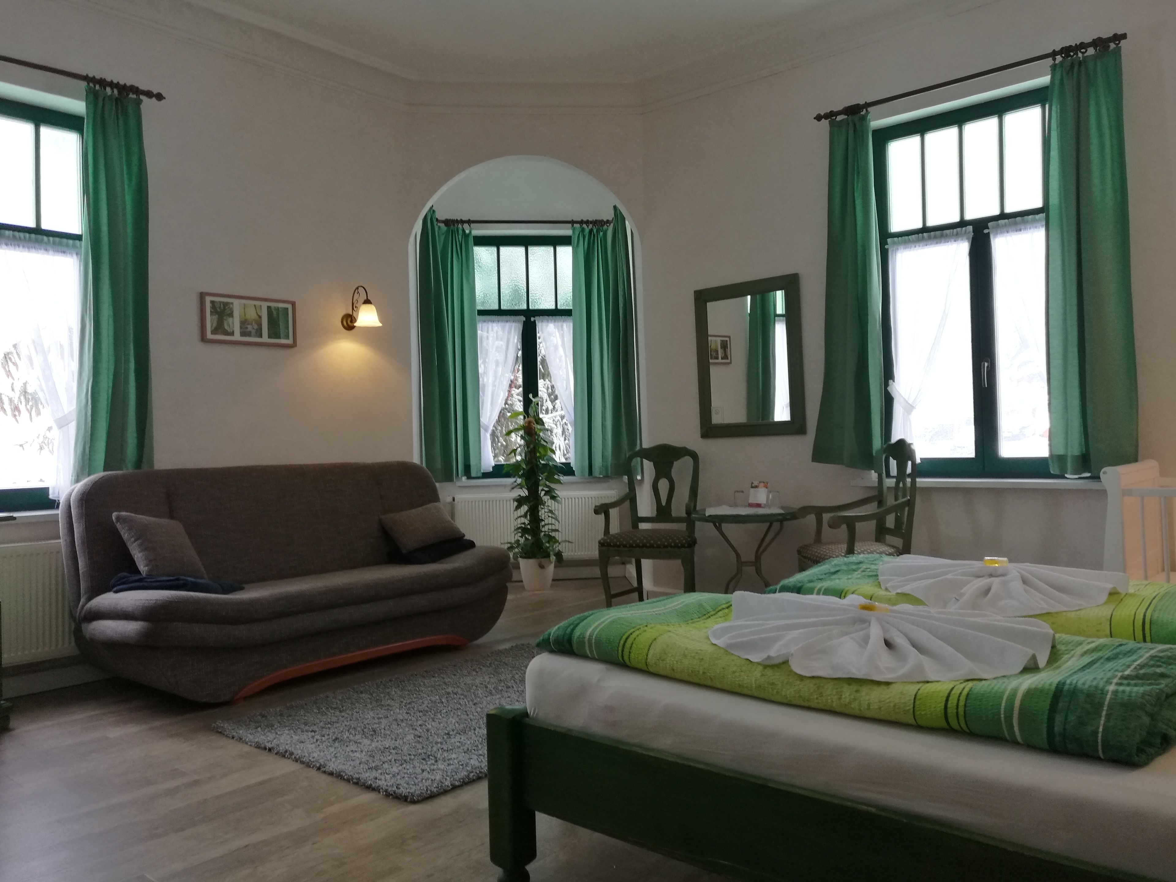Quarto com cama, sofá, poltrona, mesa e janela com cortinas.