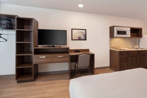 Quarto de hotel compacto com cama, escrivaninha com cadeira, TV, quadro decorativo, micro-ondas e armário embutido.