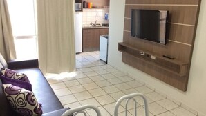 Uma sala de estar moderna com sofá, TV e cozinha ao fundo.