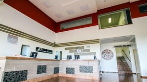Uma área de recepção com balcão de mármore, um relógio e uma escadaria que leva a um andar superior.