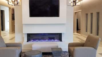 Uma sala de estar moderna com uma televisão de tela plana acima de uma lareira, dois poltronas e uma mesa de centro.