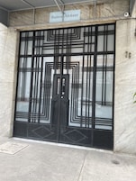 Entrada de um prédio com portão de metal e uma placa que diz 'Suites Alcazar'.