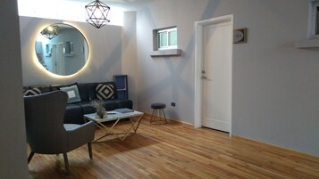Uma sala de estar moderna com um espelho redondo, um sofá com almofadas estampadas, uma mesa de centro e um banquinho.