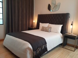Uma cama bem arrumada com um cobertor preto, uma luminária de cabeceira e um espelho na parede.