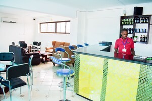 Uma área de bar com balcão, cadeiras e um espaço de estar com sofás e mesas.