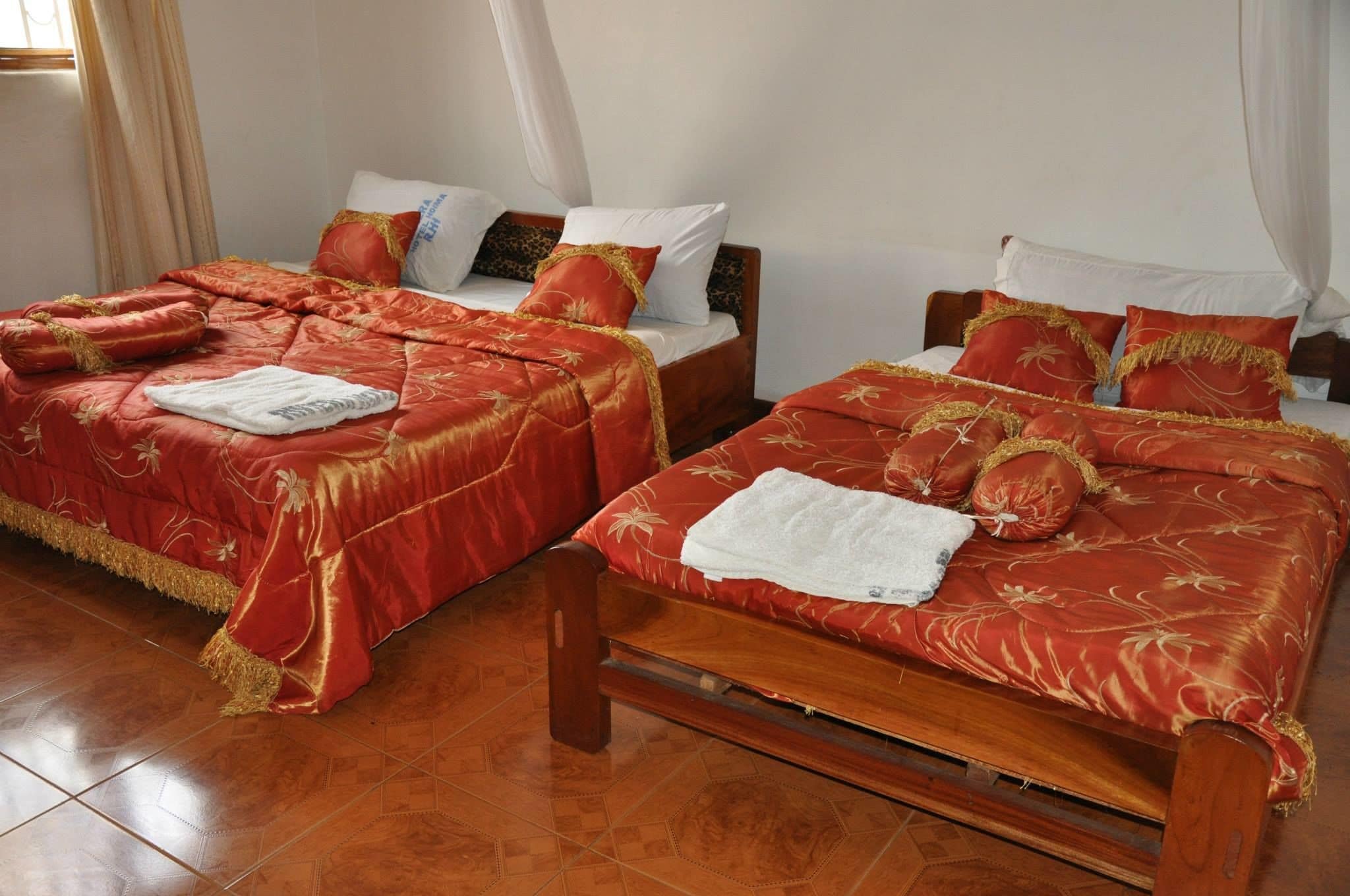Quarto de hotel com duas camas de madeira, cada uma com roupa de cama vermelha e almofadas brancas.