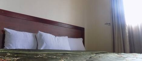 Cama com cabeceira de madeira, duas almofadas brancas e colcha verde com padrão floral.