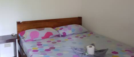 Um quarto com cama de madeira, roupa de cama estampada com bolinhas coloridas, um quadro na parede e um ventilador de teto.