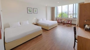 Quarto de hotel com duas camas, área de refeições e uma grande janela com vista para a cidade.