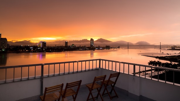 Varanda com cadeiras de madeira com vista para a cidade ao pôr do sol.