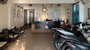Uma área de recepção com balcão, obras de arte emolduradas e uma placa com a inscrição 'VITALIS RIVERSIDE HOTEL'.