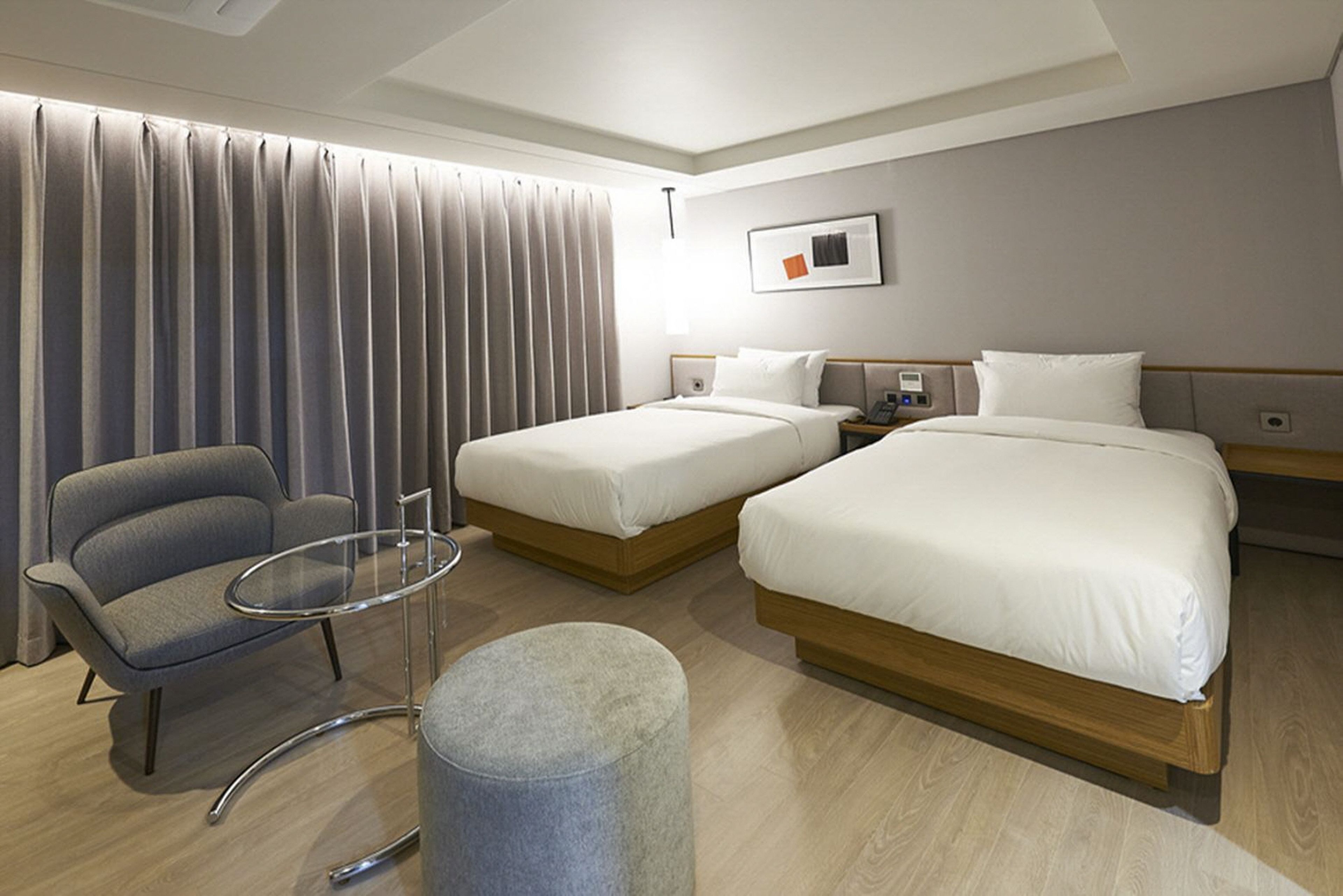 Quarto de hotel com duas camas de solteiro, um sofá, uma mesinha e uma janela grande com cortinas.