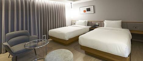 Quarto de hotel com duas camas de solteiro, um sofá, uma mesinha e uma janela grande com cortinas.