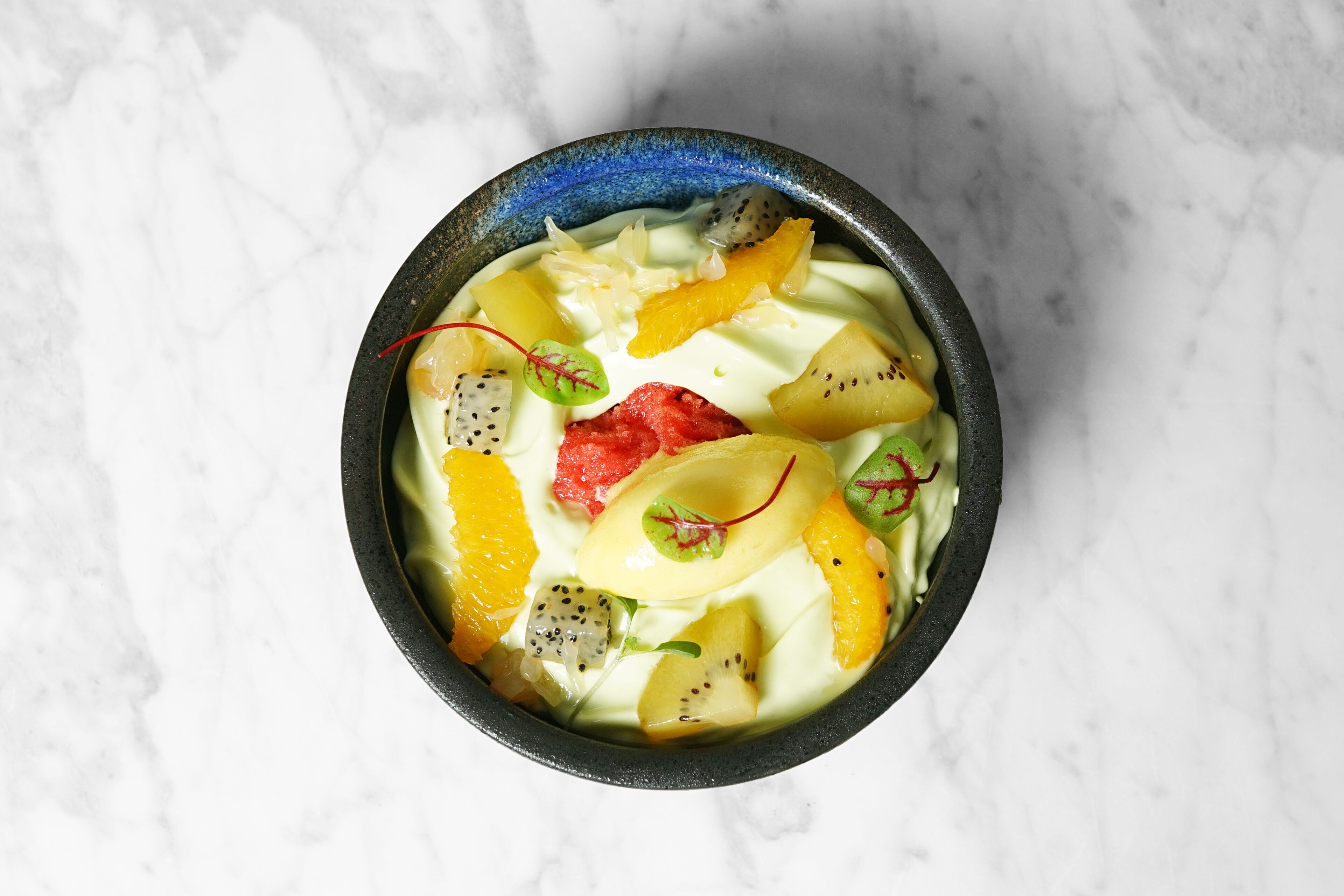 Uma saladeira com salada de frutas diversas e um molho vermelho, sobre uma superfície de mármore.