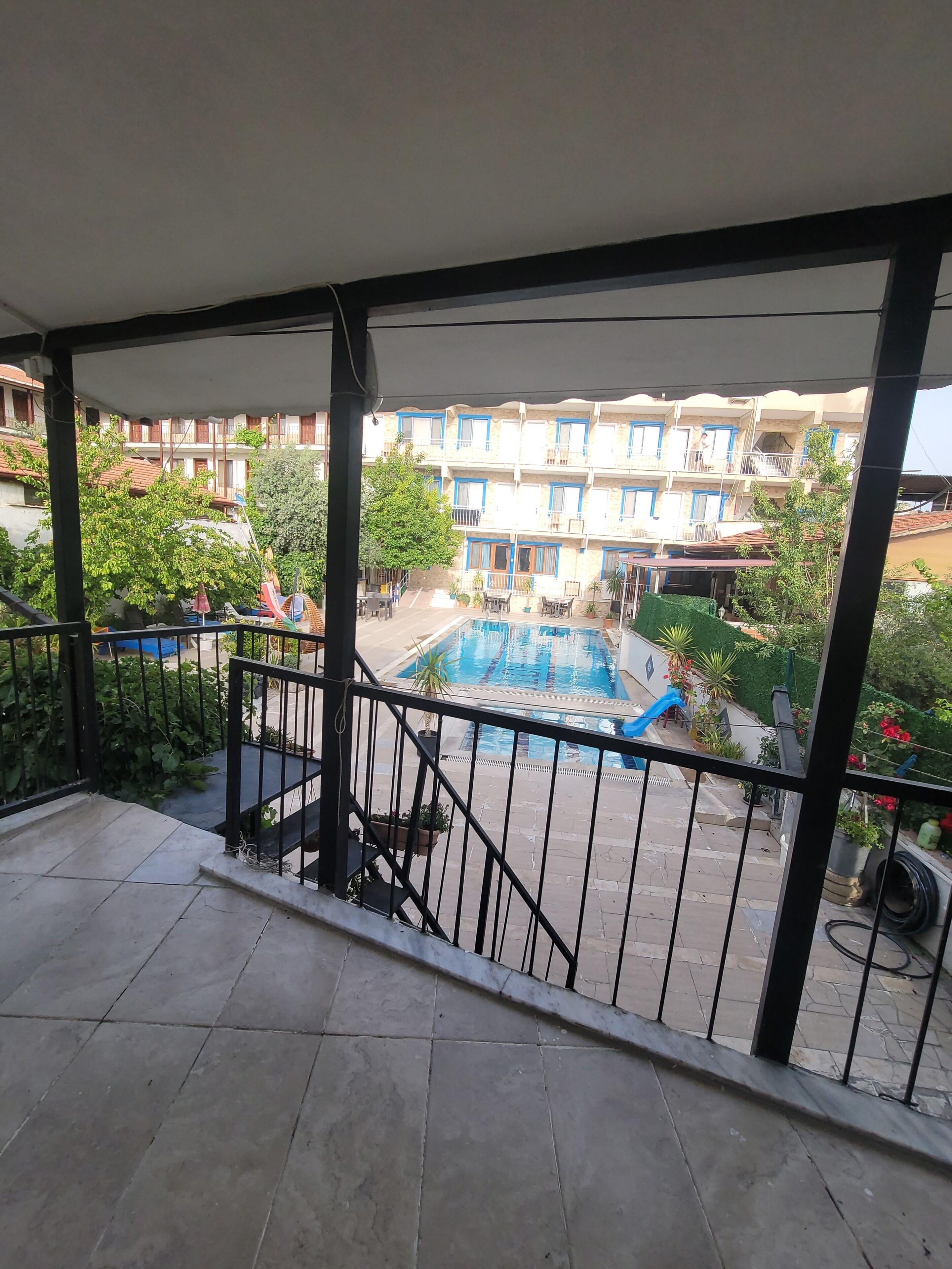 Uma varanda com vista para uma piscina, um edifício de vários andares com varandas e plantas em vasos.