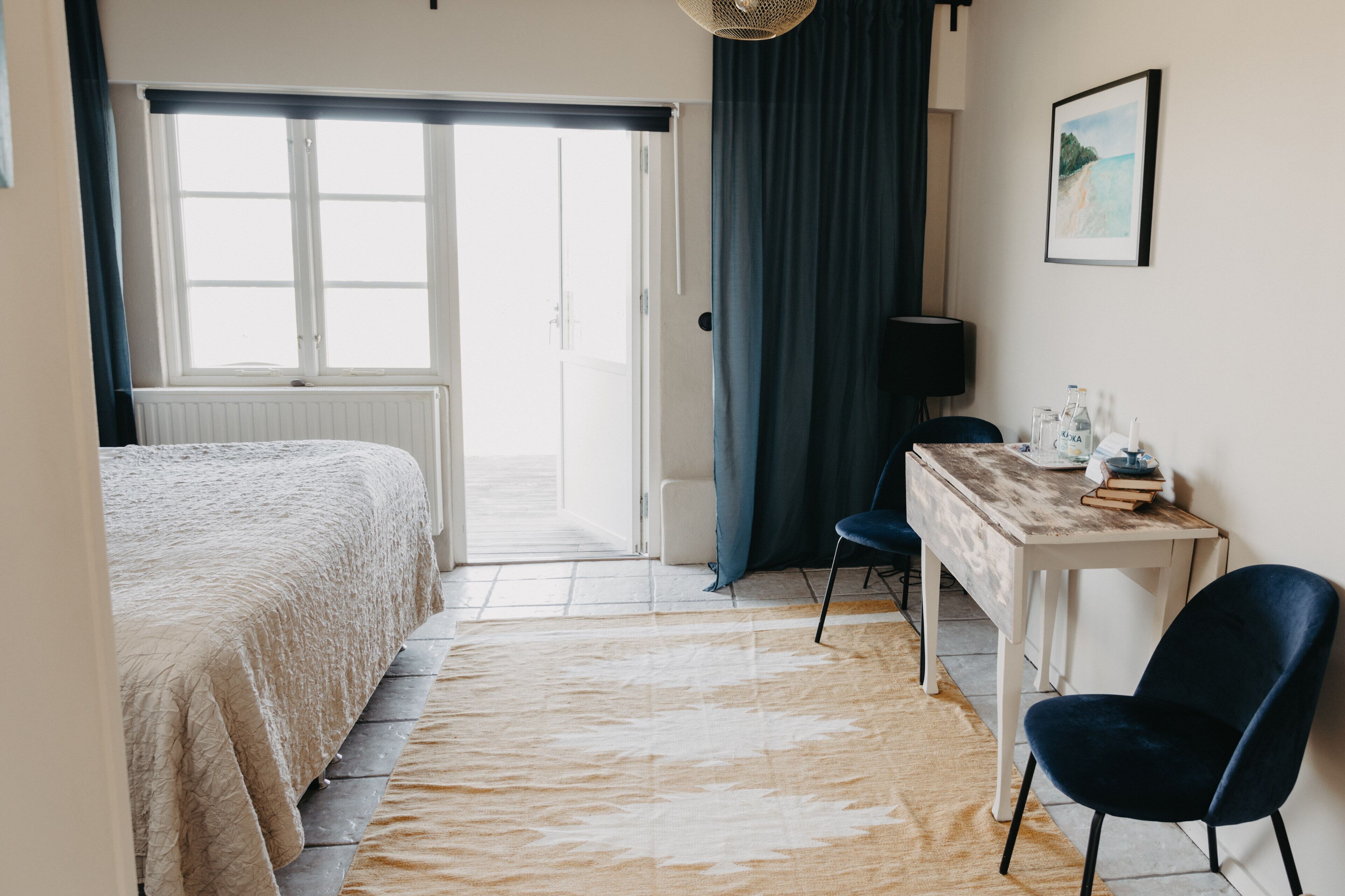 Quarto com cama, escrivaninha com cadeira, janela com cortinas e radiador.