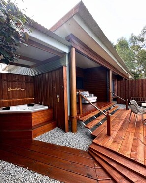 Um deck de madeira com uma banheira de hidromassagem, uma área de estar coberta e uma escadaria que leva a outro deck de madeira.