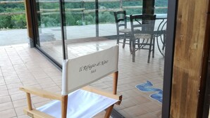 Uma cadeira de madeira com almofada branca e uma placa com a inscrição 'Il Refugio di Nino B&B' em um pátio de azulejos com vista para colinas verdes.
