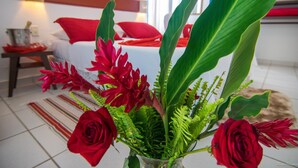 Quarto de hotel com uma cama, uma mesa de cabeceira e um vaso com flores vermelhas.