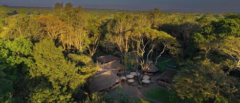 Vista aérea de uma pousada rodeada por floresta densa, com várias cabanas de telhado de palha e uma área central aberta com assentos.
