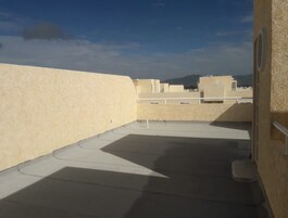 Terraço no telhado com piso de concreto, paredes bege e vista para outros edifícios e montanhas ao longe.
