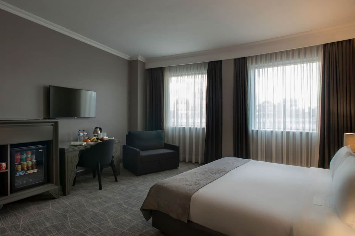 Quarto de hotel com cama, escrivaninha, cadeira, televisão e minibar.