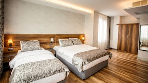 Quarto de hotel moderno com duas camas, piso de madeira e um espelho grande.