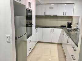 Uma cozinha moderna com armários brancos, eletrodomésticos de aço inoxidável e bancada preta.