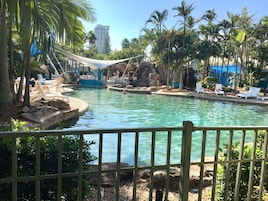 Área de piscina com espreguiçadeiras, palmeiras e paisagem rochosa.
