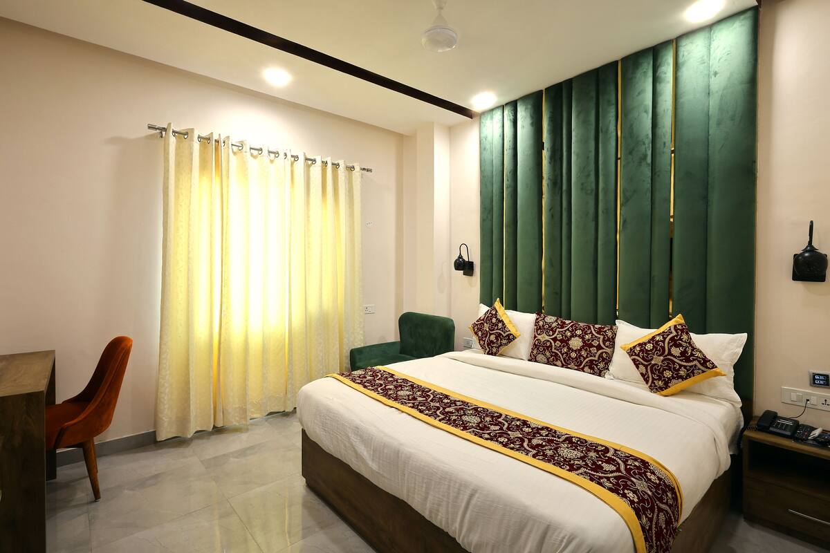 Quarto de hotel com uma cama grande, uma escrivaninha, uma cadeira e cabeceira verde.