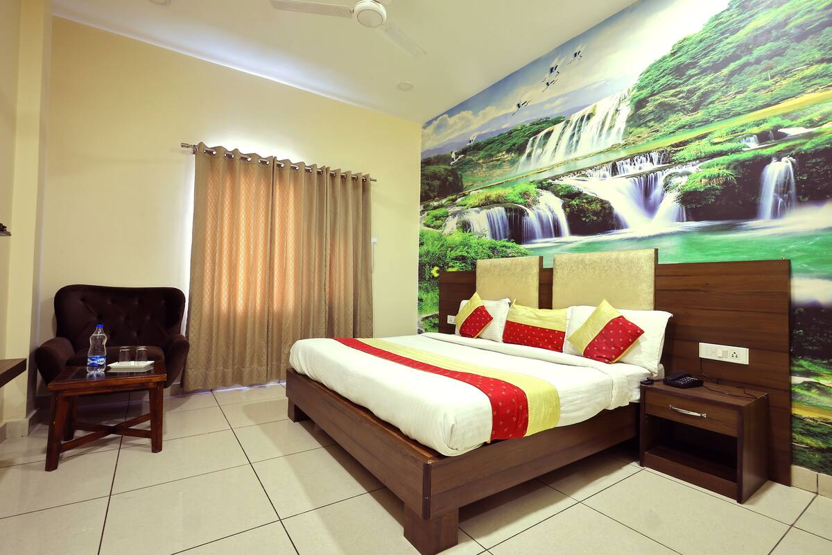 Quarto de hotel com uma cama grande, uma mesa de cabeceira, uma cadeira e uma mesa com garrafa e copos.