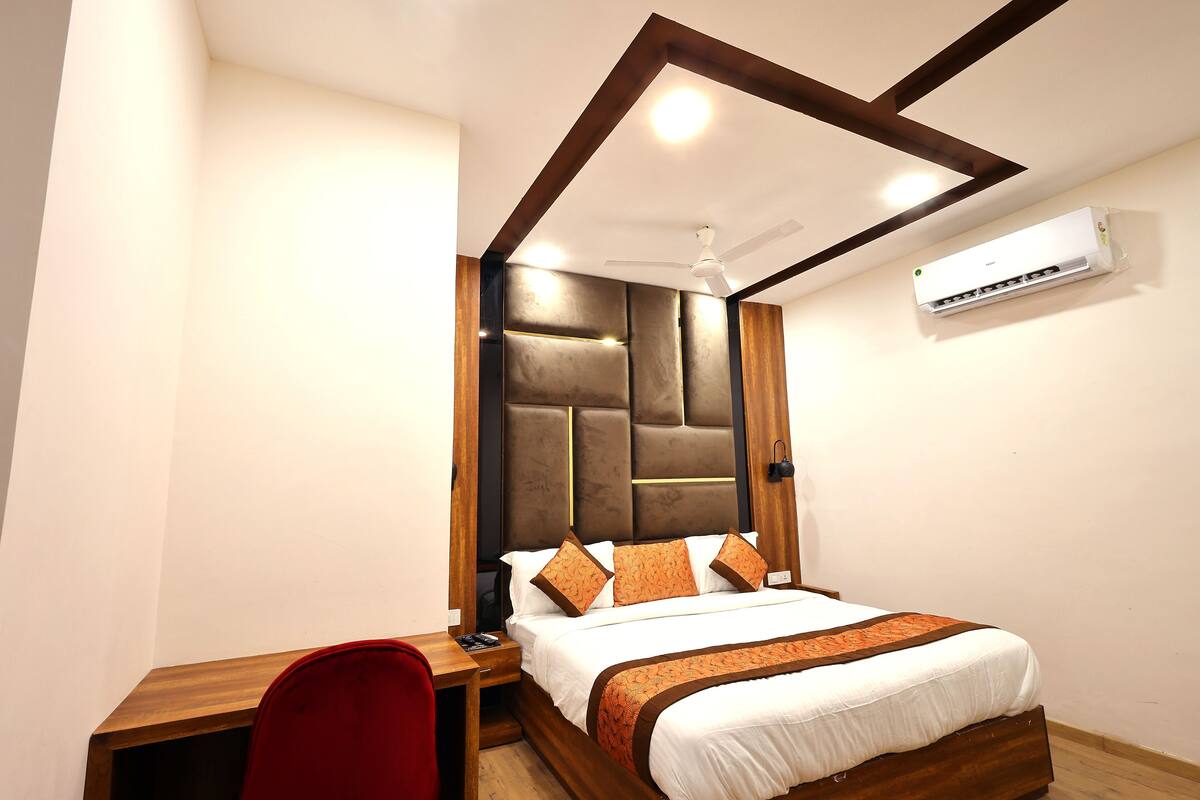 Quarto de hotel moderno com cabeceira de madeira, uma escrivaninha e uma cadeira vermelha.