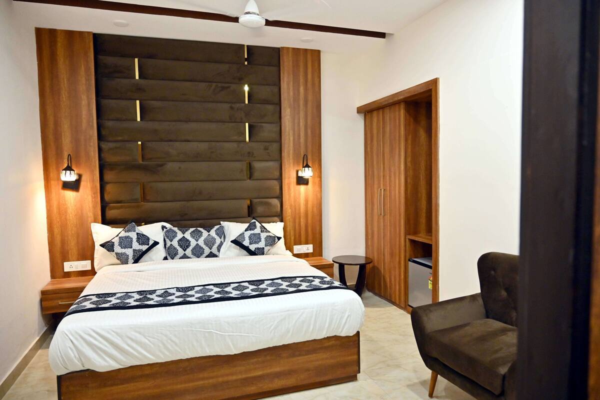 Quarto com uma cama grande, cabeceira de madeira, duas luminárias de cabeceira, uma mesinha, uma cadeira e um guarda-roupa.