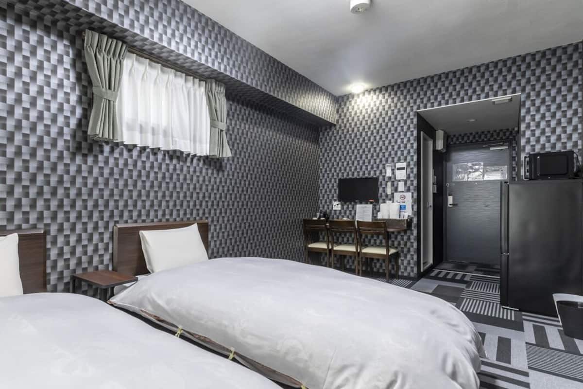 Quarto de hotel com padrão de parede quadriculado, uma cama com roupa de cama branca, uma escrivaninha com cadeira, uma televisão e um frigorífico.