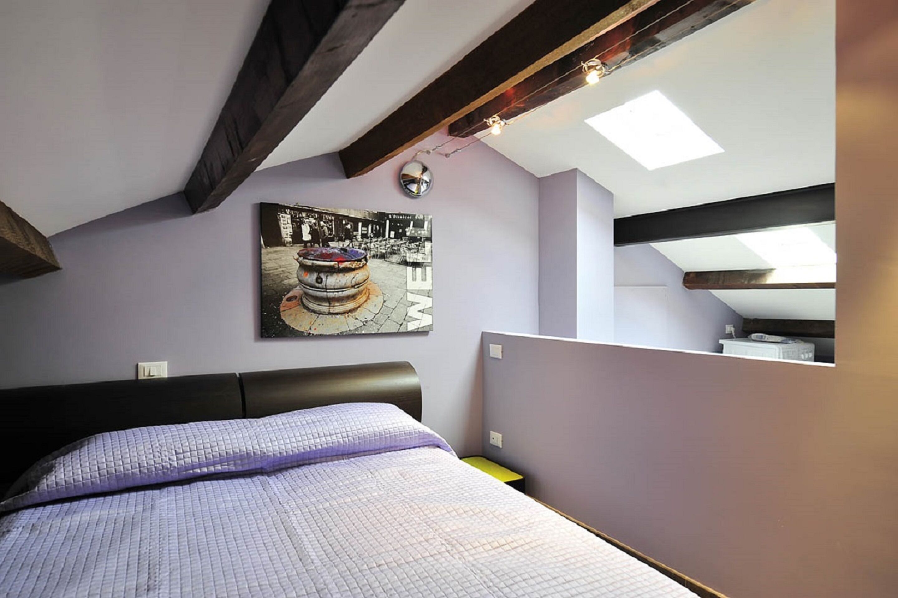 Quarto moderno com cama, uma grande obra de arte na parede e um claraboia.