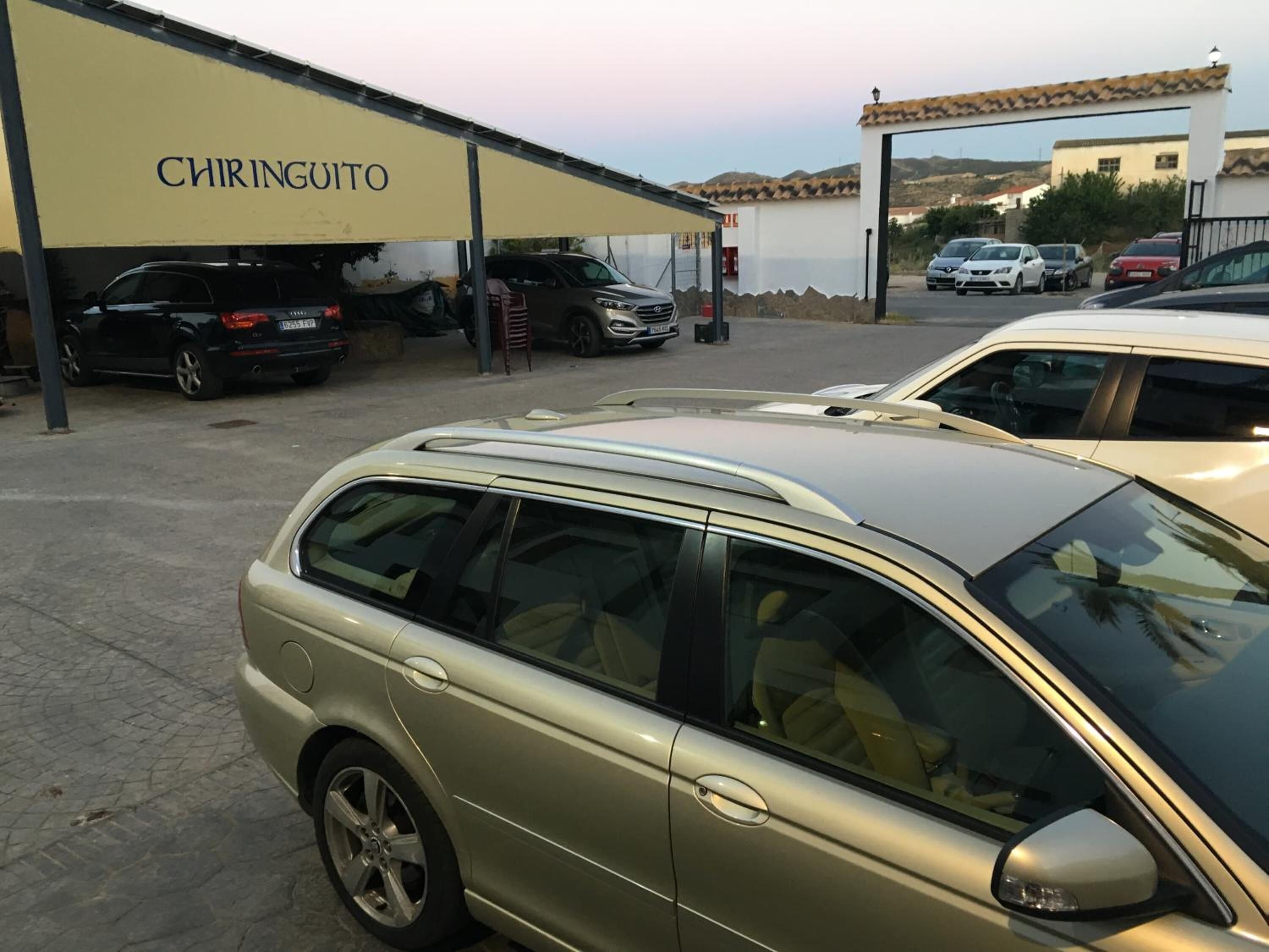 Uma área de estacionamento com vários carros, incluindo uma carrinha bege e um SUV preto.