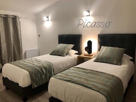 Quarto de hotel com duas camas, uma luminária na parede e uma cortina.