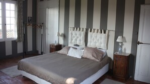 Um quarto com uma cama grande, paredes listradas, um guarda-roupa e uma janela com cortinas.