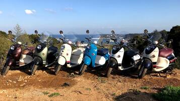 Fileira de scooters estacionadas numa trilha de terra com vista panorâmica de uma cidade costeira ao fundo.