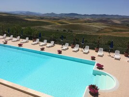 Piscina com espreguiçadeiras e plantas em vasos, com vista panorâmica de colinas ondulantes e turbinas eólicas.