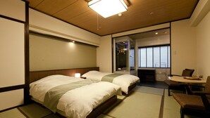 Quarto tradicional japonês com tatames, duas camas, um pequeno espaço de refeições e uma porta de vidro deslizante para uma varanda.