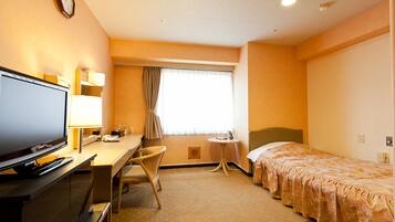 Quarto de hotel com cama, escrivaninha, cadeira, televisão, mesa pequena e janela com cortinas.