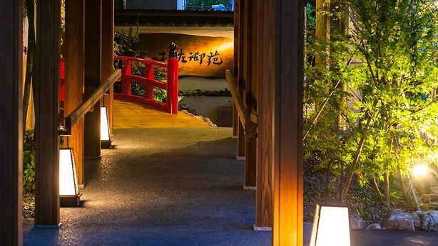 Um portão japonês tradicional com pilares vermelhos e uma passarela de madeira que leva a um edifício.