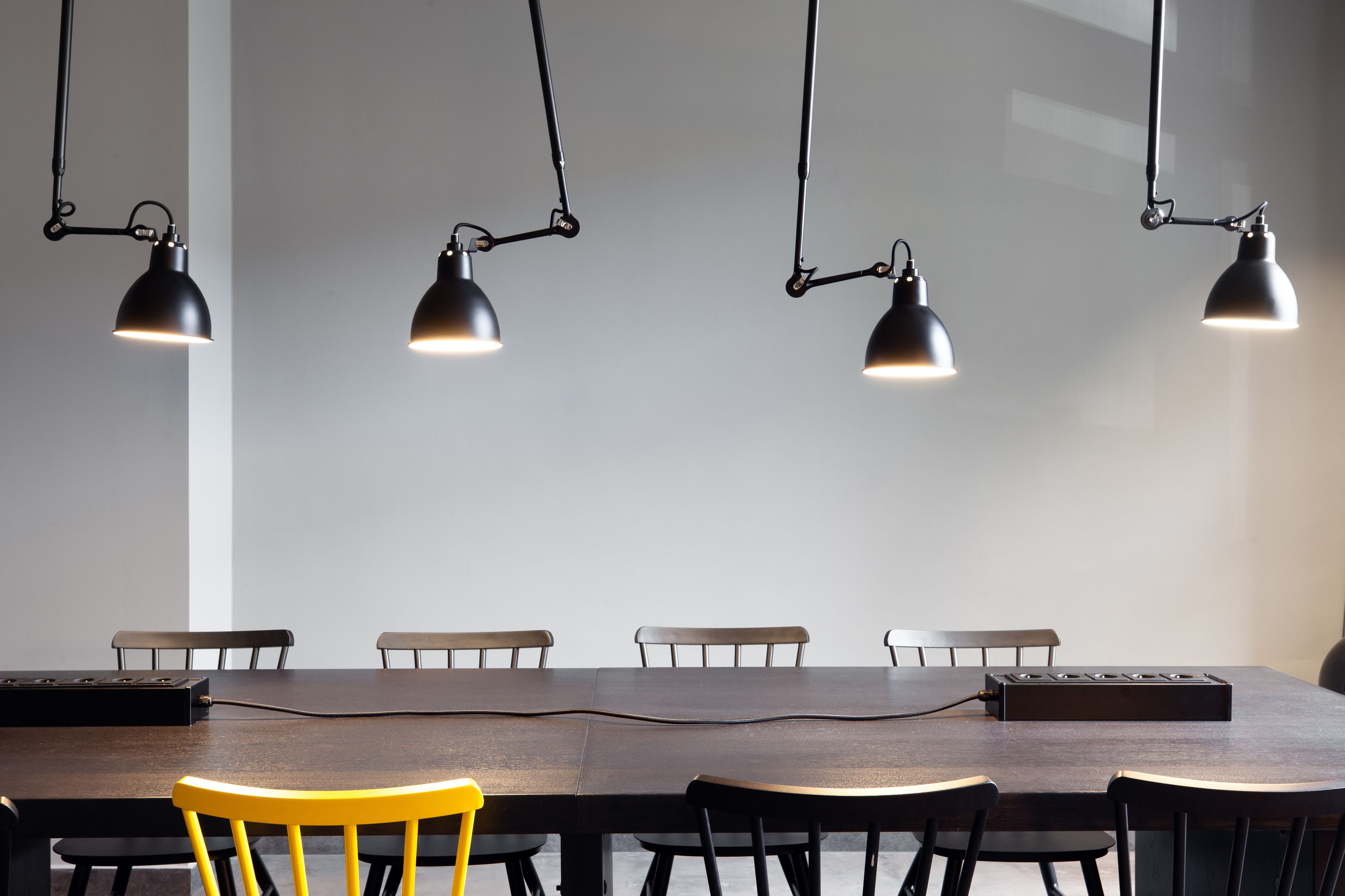 Uma sala de conferências com uma mesa comprida, várias cadeiras e luminárias pendentes.