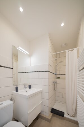 Uma casa de banho moderna com lavatório branco, espelho e chuveiro.