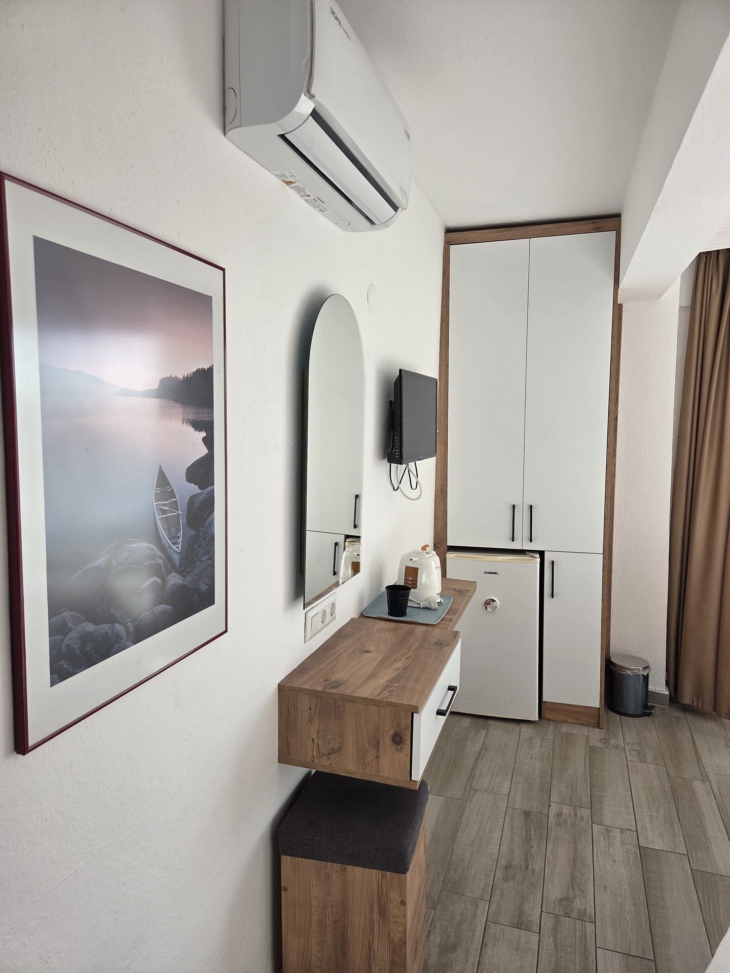Quarto de hotel moderno com uma secretária de madeira, uma televisão montada, um quadro emoldurado e um guarda-roupa.