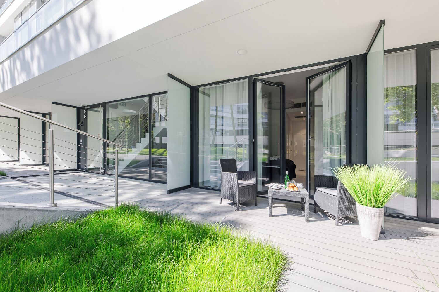 Uma área externa moderna com assentos, portas de vidro, uma escada e uma pequena mesa com uma planta.
