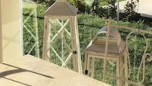 Vista pela janela com um jardim, apresentando um lanterna branca e um corrimão de metal.