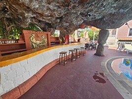 Uma área de bar ao ar livre com parede de pedra, banquetas e piscina.