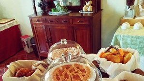 Uma mesa de buffet com diversos produtos de panificação e pastelaria, incluindo tortas e croissants, cobertos por cúpulas de vidro e servidos em cestos de tecido.